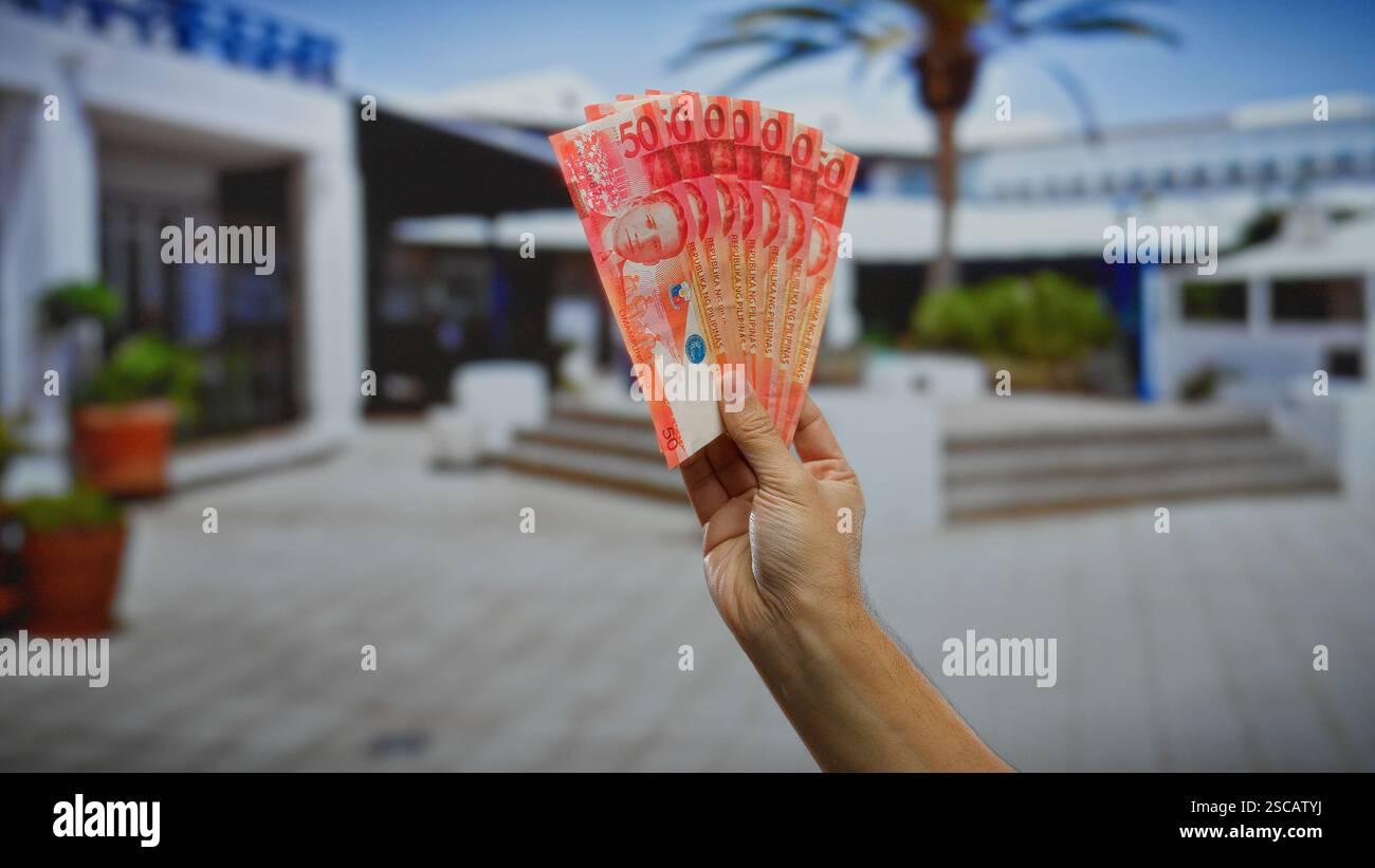 Hand clutching philippine pesos in an outdoor urban setting, showcasing ...
