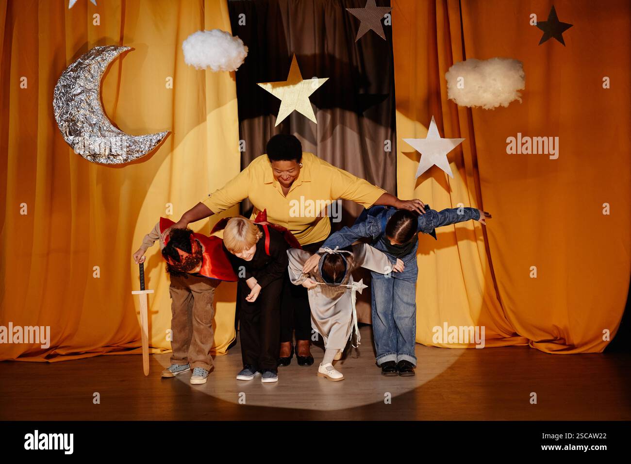 Group of children, led by their teacher, bowing to audience on stage ...