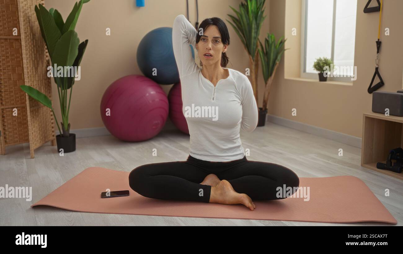Young woman stretching indoors at a gym surrounded by fitness equipment ...