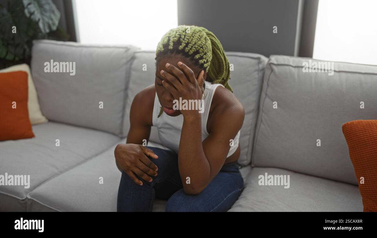 Woman sitting on a sofa in a living room, visibly worried, with her ...