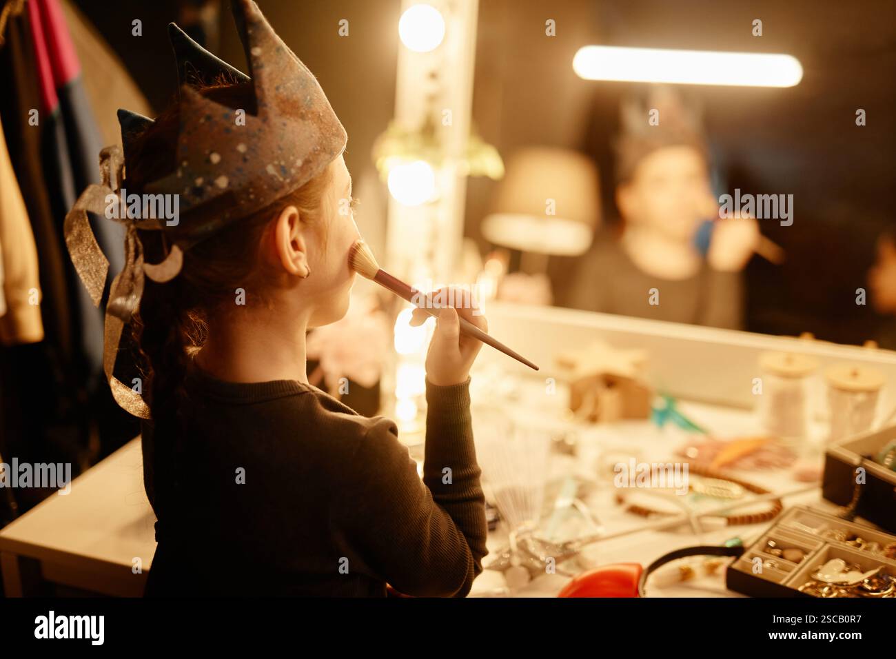 Child wearing costume headpiece and applying makeup in dressing room ...