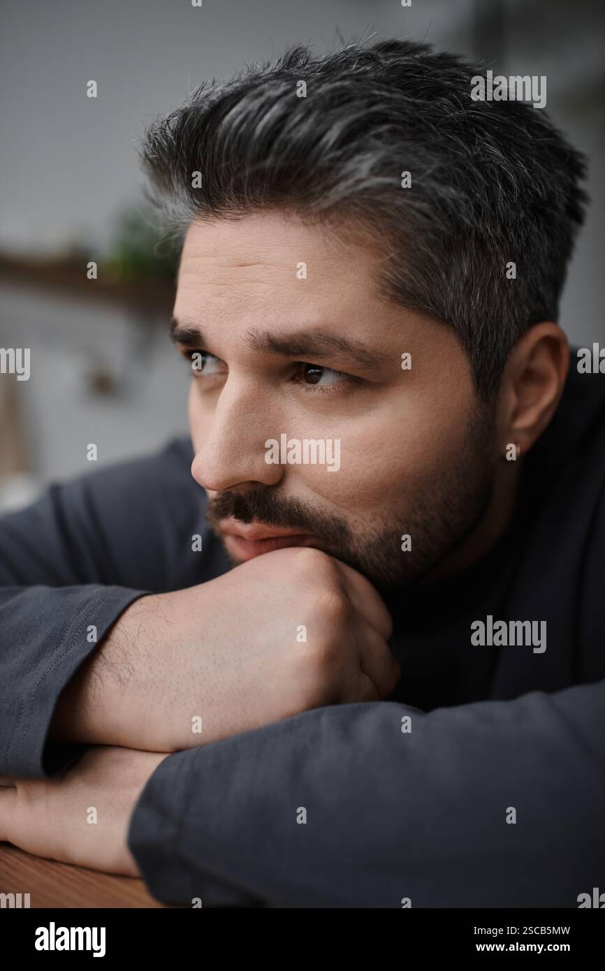 A handsome man looks thoughtful, resting his chin on his hand in a warm ...