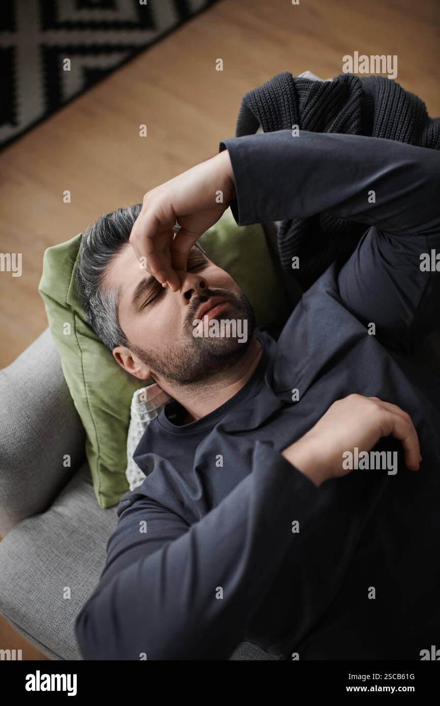 A handsome man lies comfortably on a couch, resting his forehead in ...