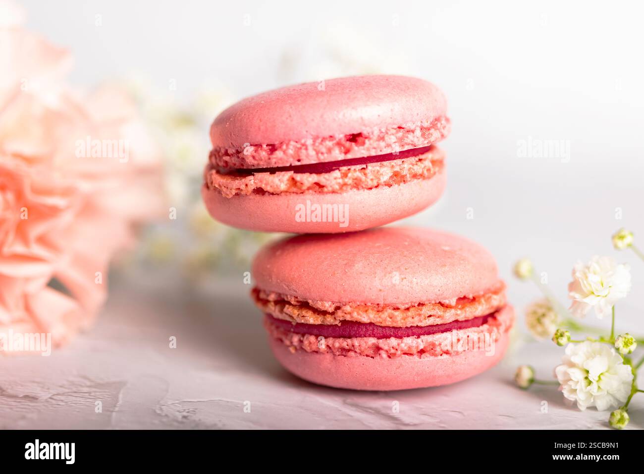 Two pink macarons on top of each other with some pink and white flowers ...