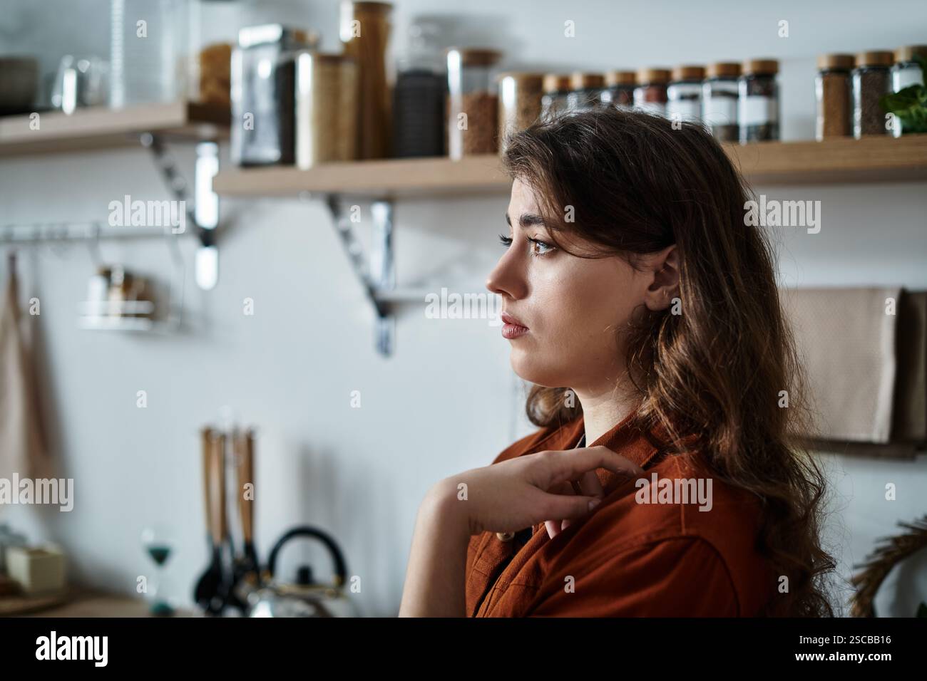 A woman stands thoughtfully in a warm kitchen, grappling with feelings ...