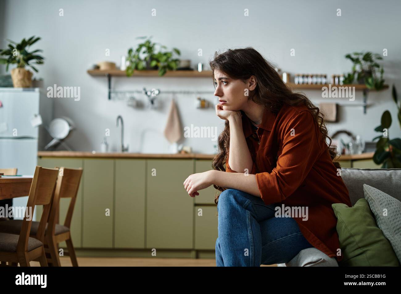 A woman sits on her couch, lost in thought, overwhelmed by sadness Stock Photo - Alamy