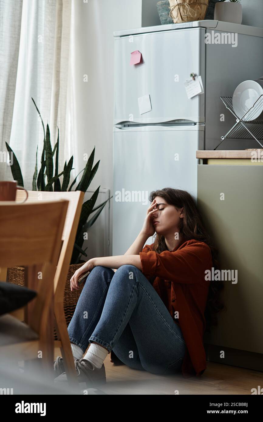 In a cozy kitchen, a woman leans against the wall, her face showing ...