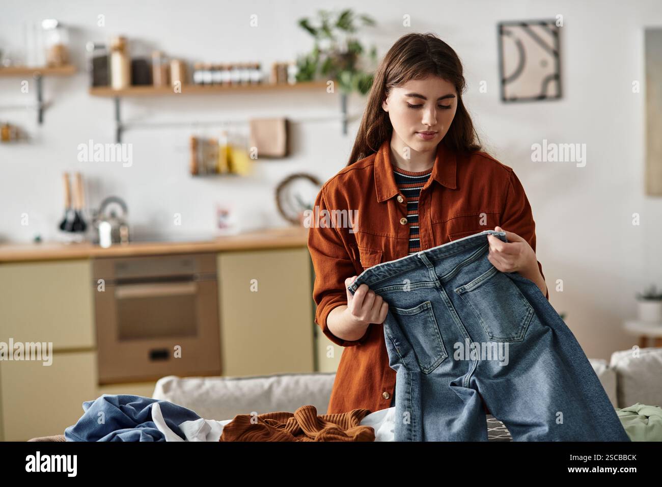 A young woman reflects on her feelings as she organizes clothing in a ...