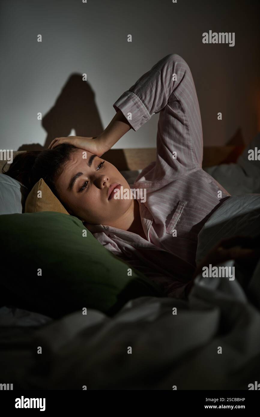 A woman lies awake in bed, overwhelmed by thoughts and emotions in ...