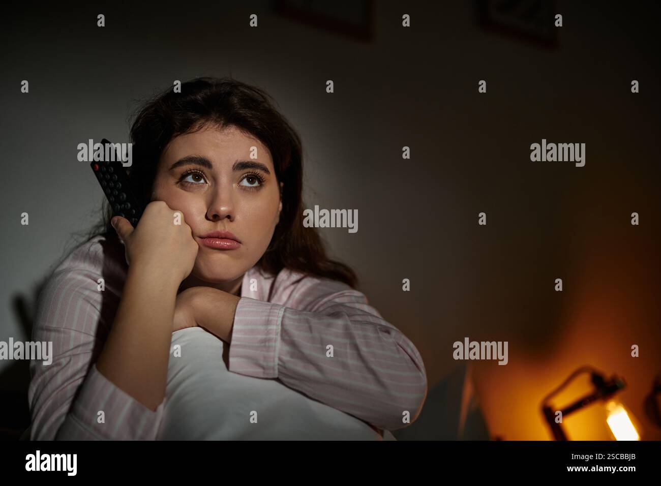 A woman sits alone in a dim room, lost in thought and grappling with her feelings Stock Photo ...