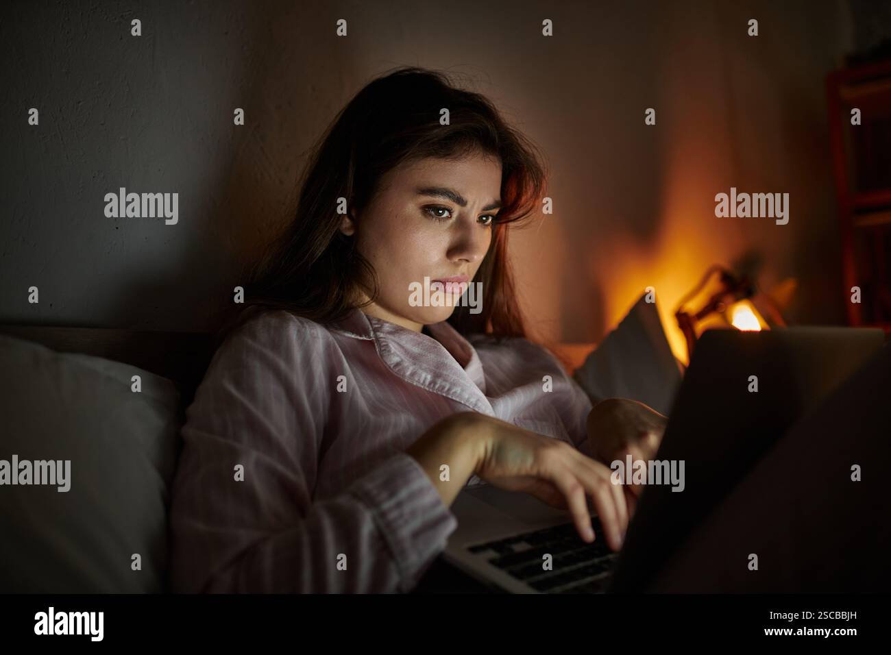 In a dimly lit room, a woman sits on her bed, deeply absorbed in her ...