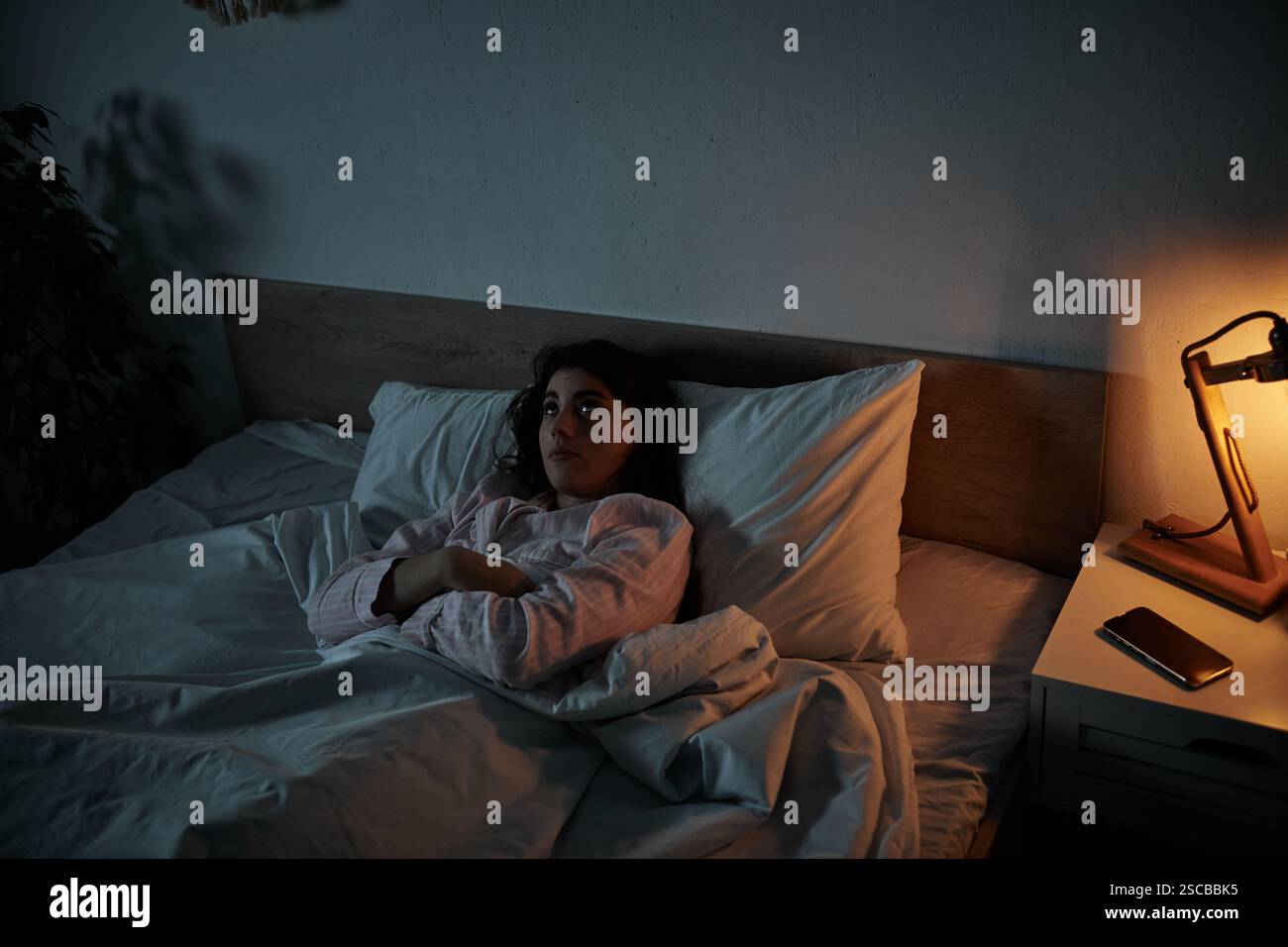 A woman lies in bed, wrapped in blankets, lost in thought as she stares ...