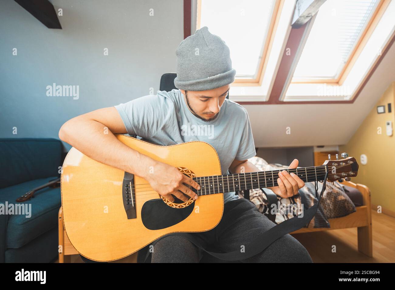 Musician sits by a sunlit window, deeply focused on playing an acoustic ...