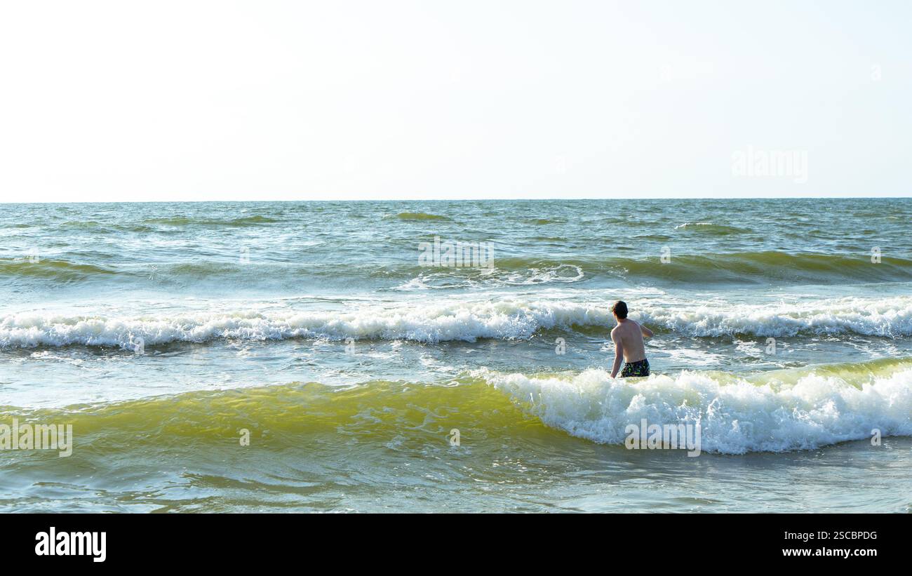 Teenager or a young man enters the waves with white foam on the Baltic ...