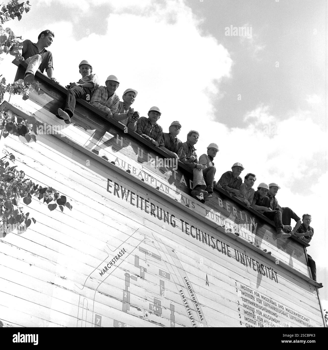 "A group of men wearing construction helmets sit on a sign to see the ...