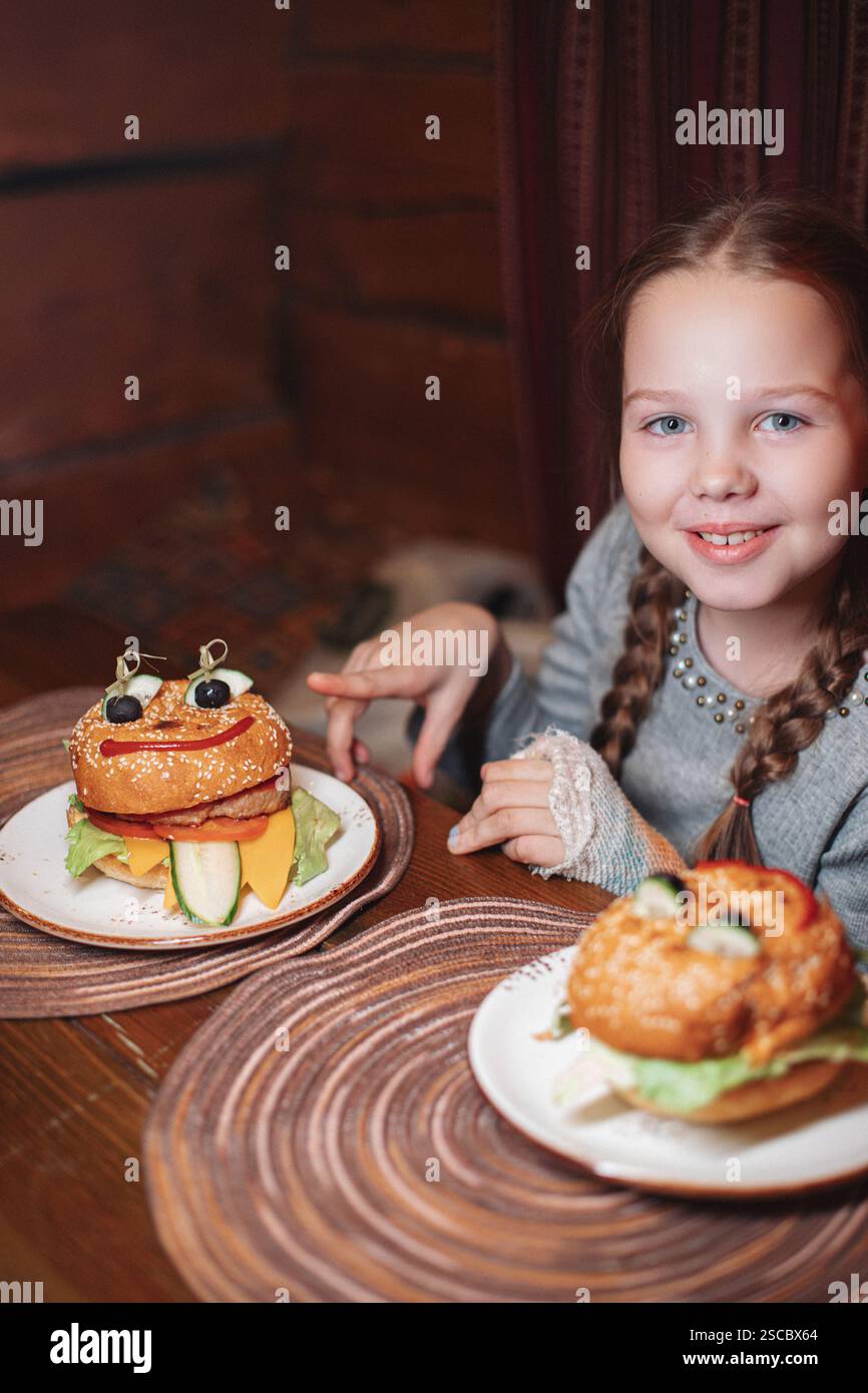 A girl child is sitting in a cafe and is going to eat a burger. A kid's ...