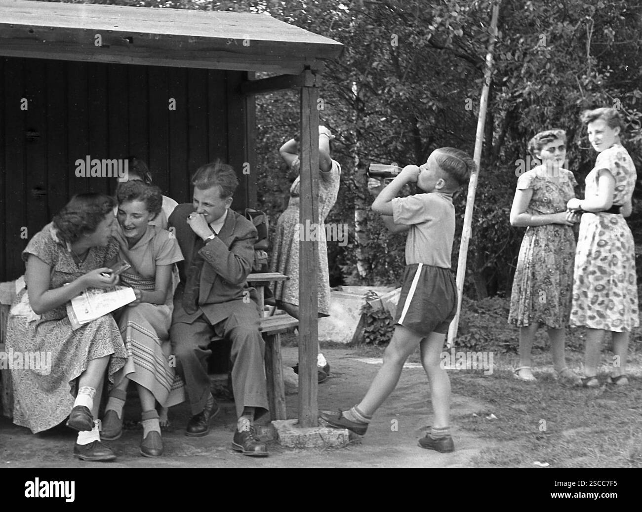 People sitting and standing wait at a bus stop for the bus. Left side ...