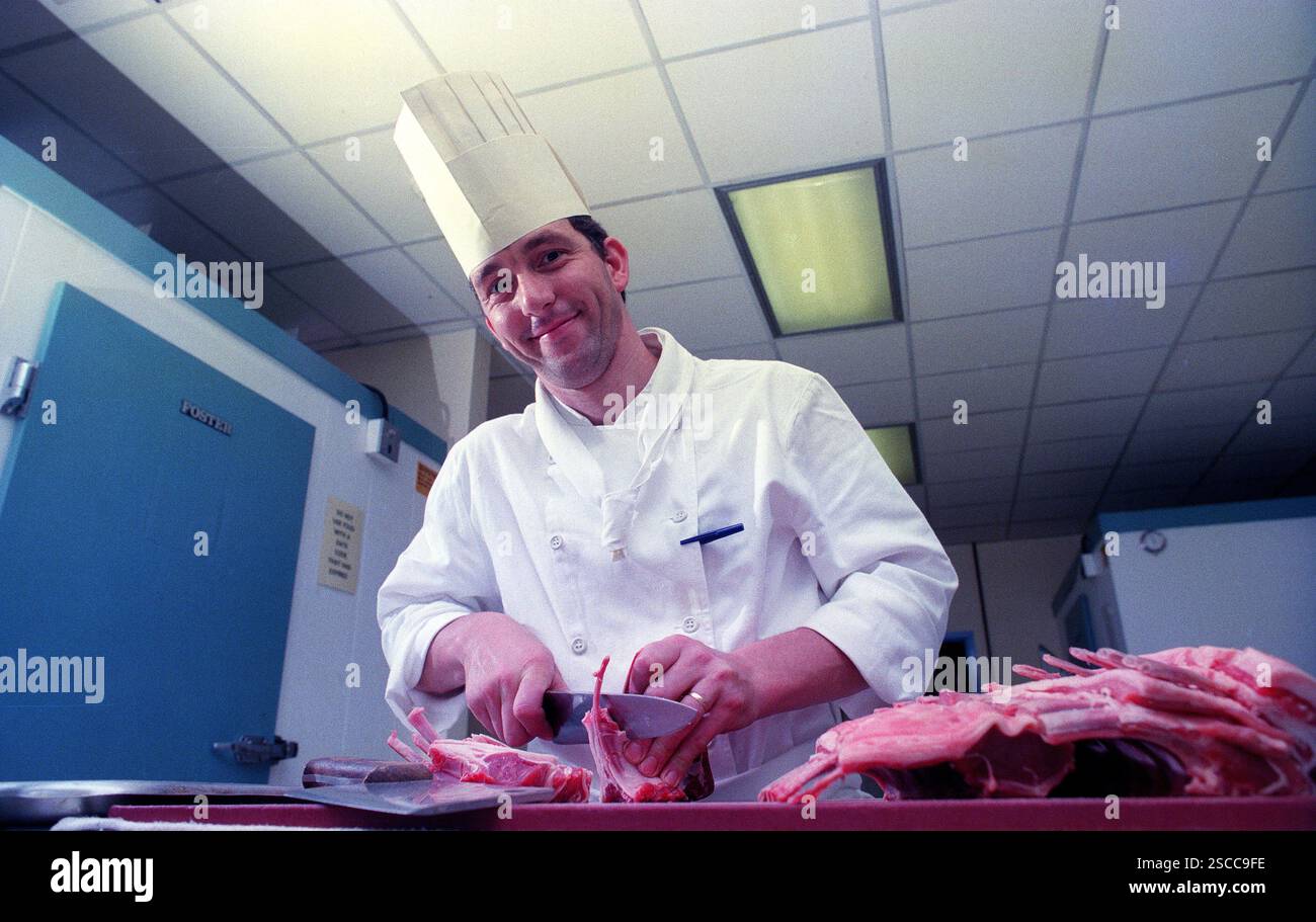 A head chef wearing the traditional toque hat preparing meat cuts in an ...