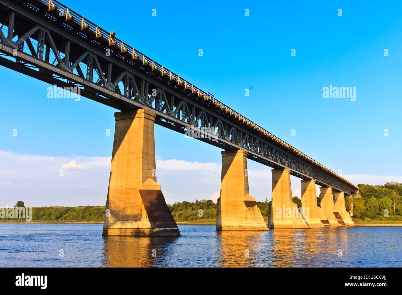 Bridge spans a river with a clear blue sky above. The bridge is made of ...