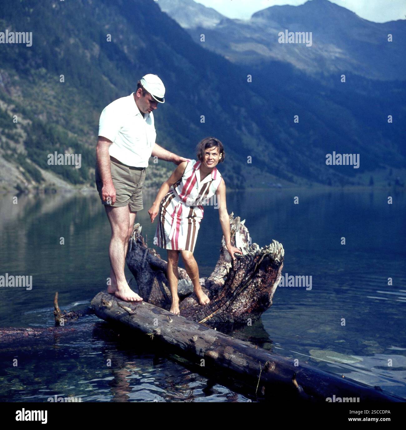 A man holds on to a woman's shoulder while balancing over a tree trunk ...