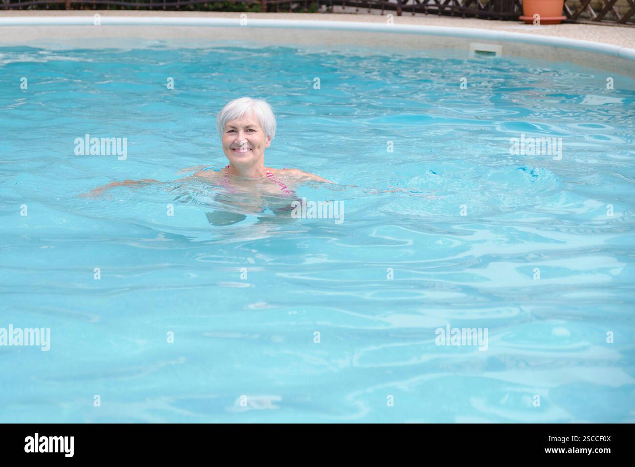 Smiling senior woman with short white hair enjoying a swim in clear ...