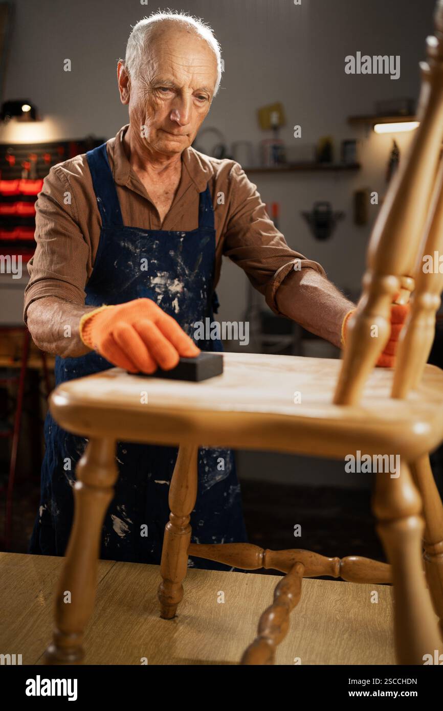 Elderly male carpenter sanding old chair with sanding sponge ...