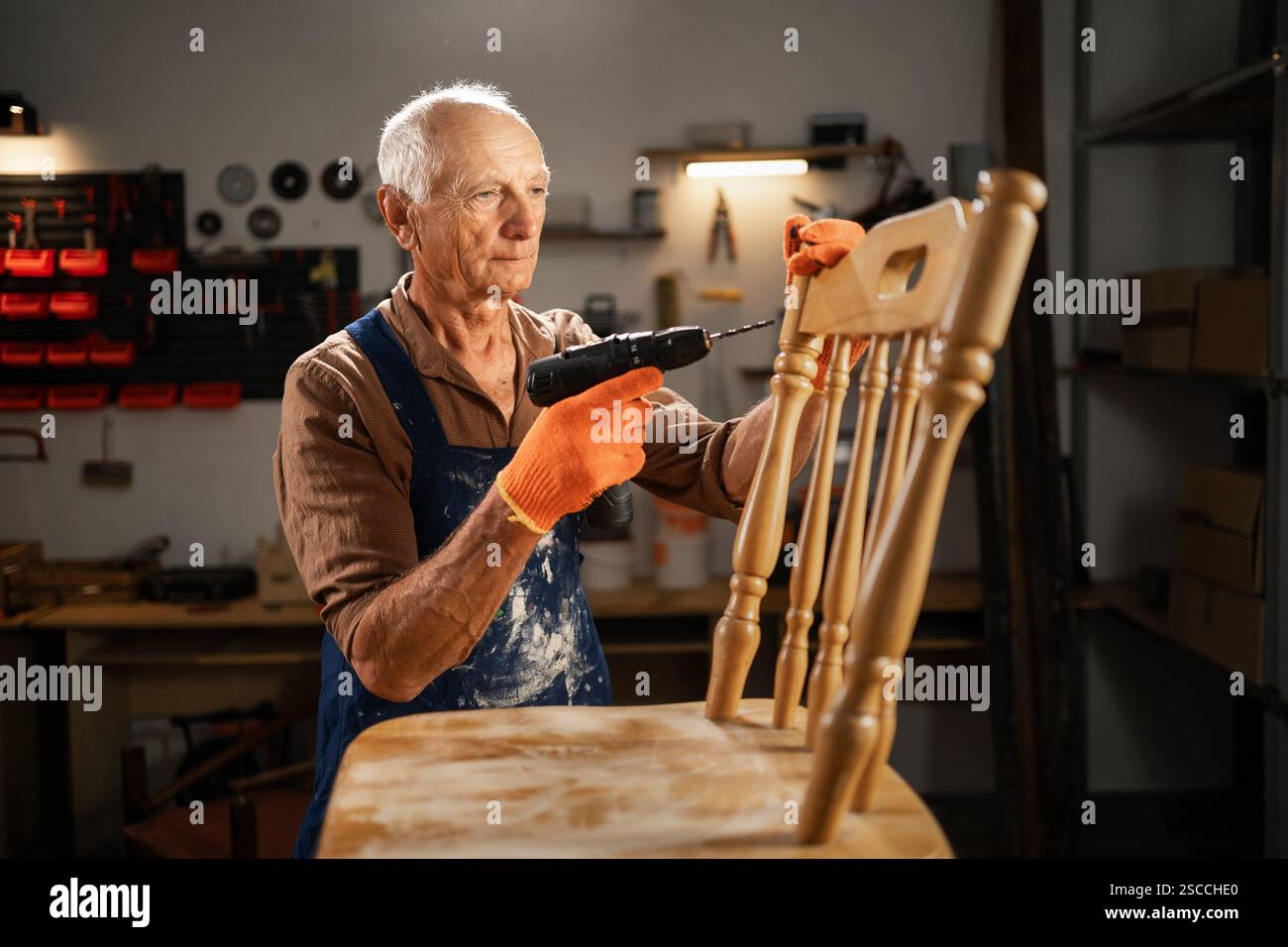Elderly man using drill to repair wooden chair Stock Photo - Alamy
