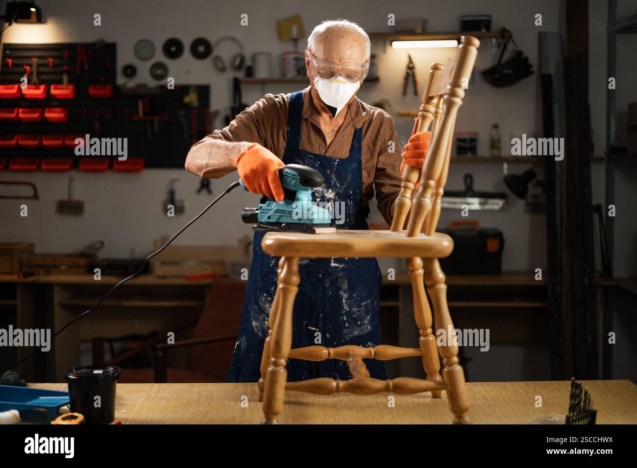 Senior man carpenter grinding wood chair with sandpaper in diy workshop ...