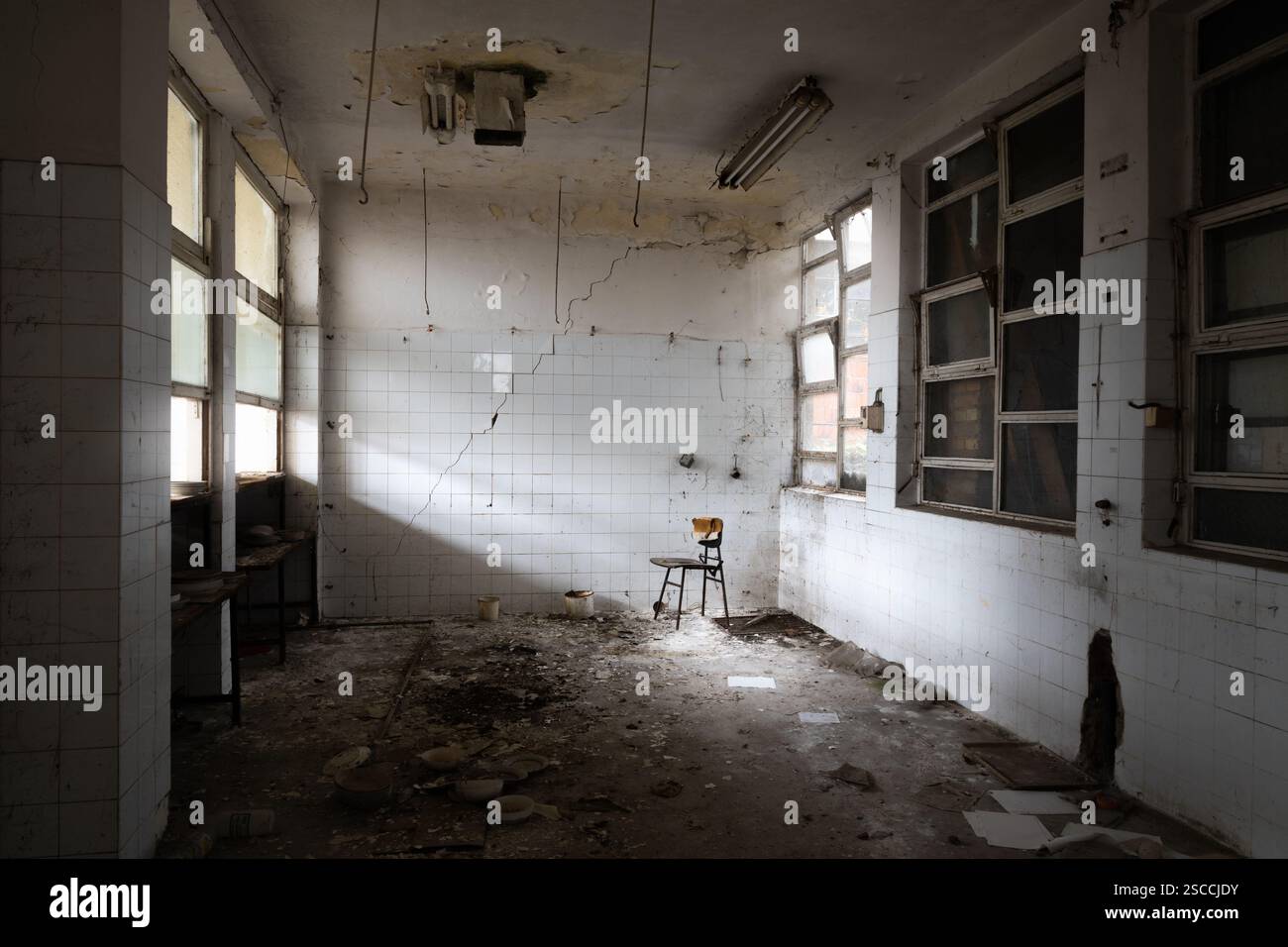 Abandoned empty kitchen with chair in corner in direct daylight, dishes ...