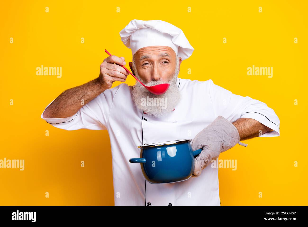 Elderly male chef in white uniform tasting food with vibrant yellow ...