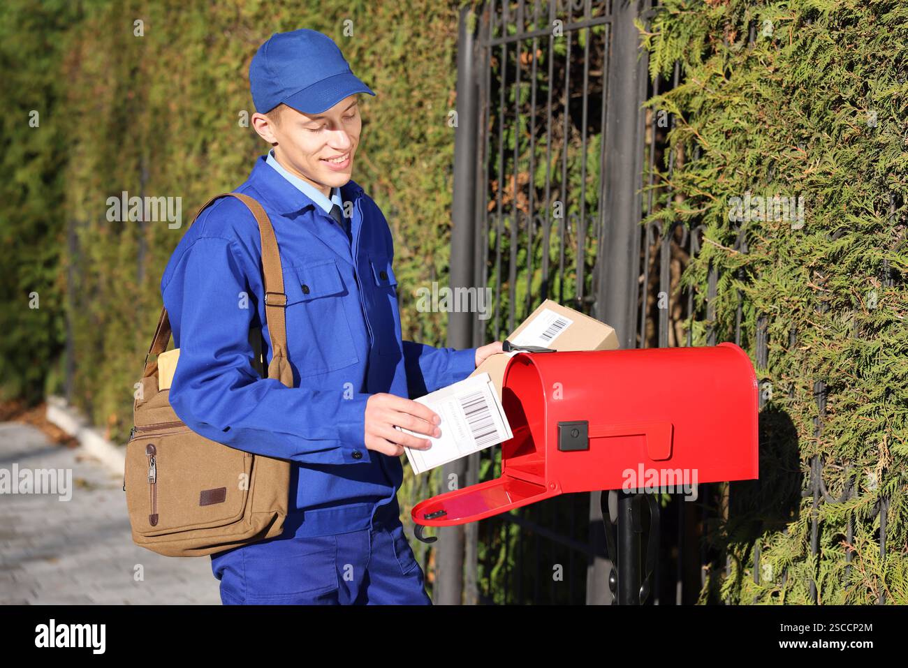 Postman putting parcel into mail box outdoors Stock Photo - Alamy