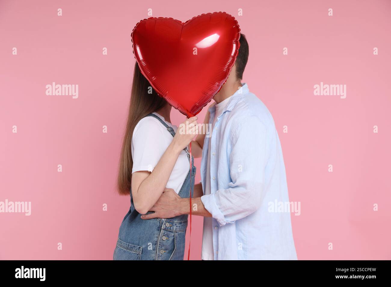 Lovely couple kissing behind heart shaped balloon on pink background ...