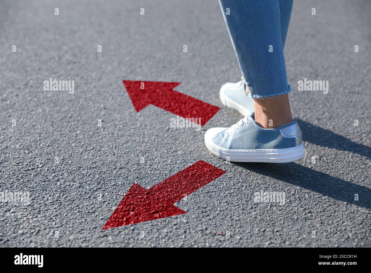 Woman walking on asphalt road with red arrows pointing in different ...