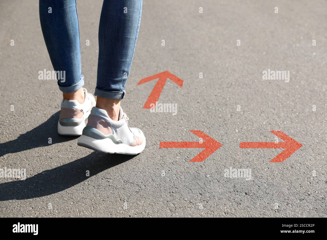 Woman walking on asphalt road with orange arrows pointing in different ...