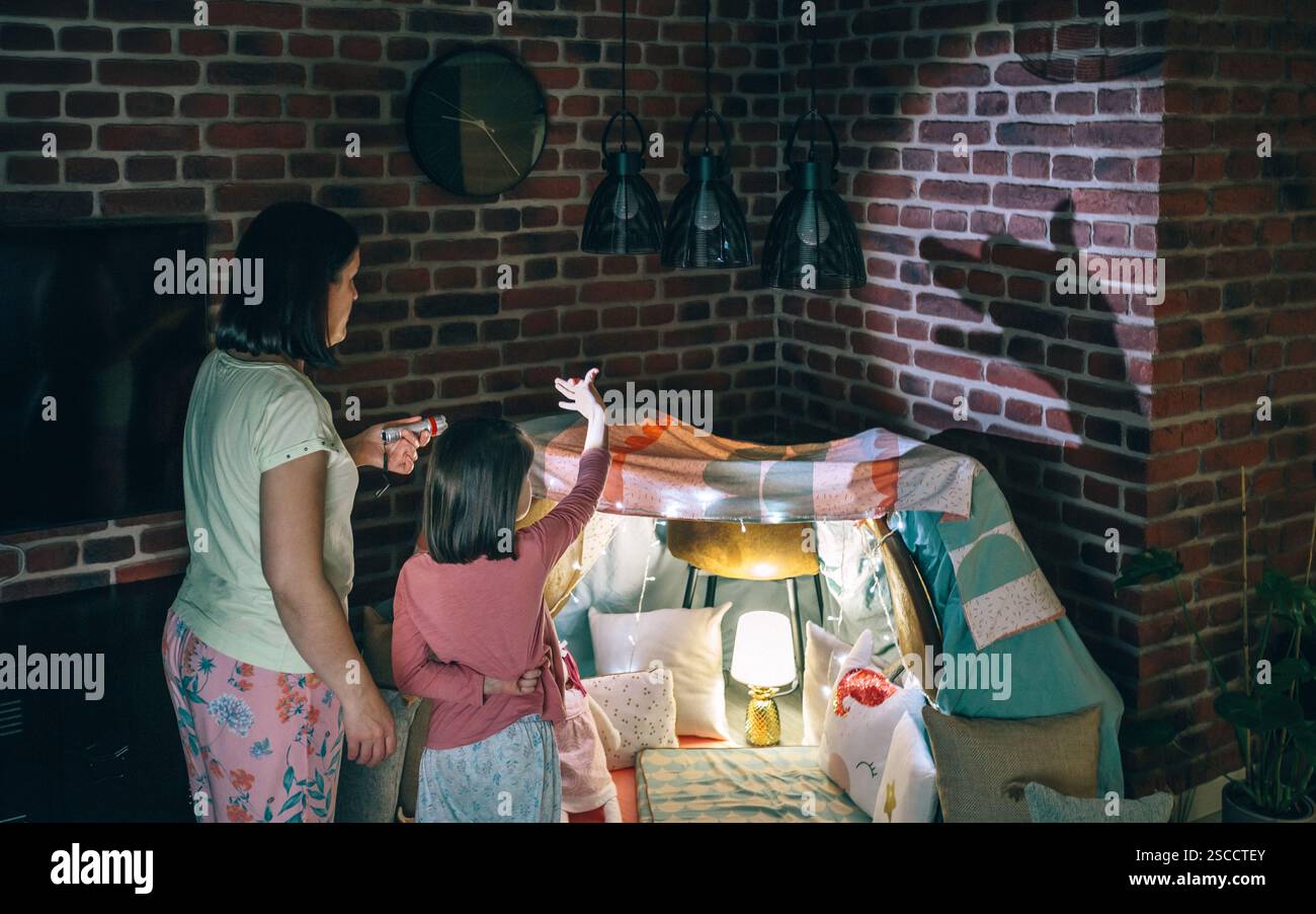 Back view of mother holding flashlight while daughter making shadow ...