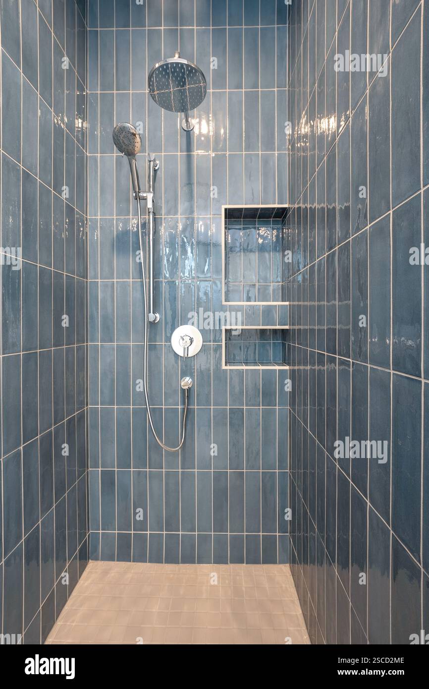 A blue tiled shower with a silver shower head. The shower is clean and ...