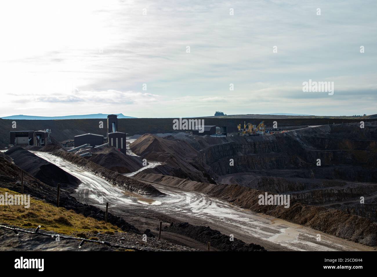 An open-pit quarry displays dark brown and black earth, heavy machinery ...