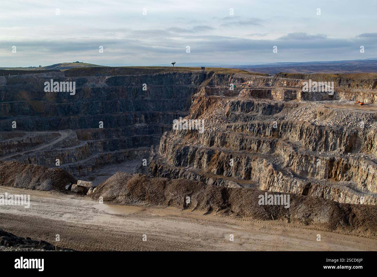 Aerial view of a large, terraced quarry with exposed rock strata. Muddy ...