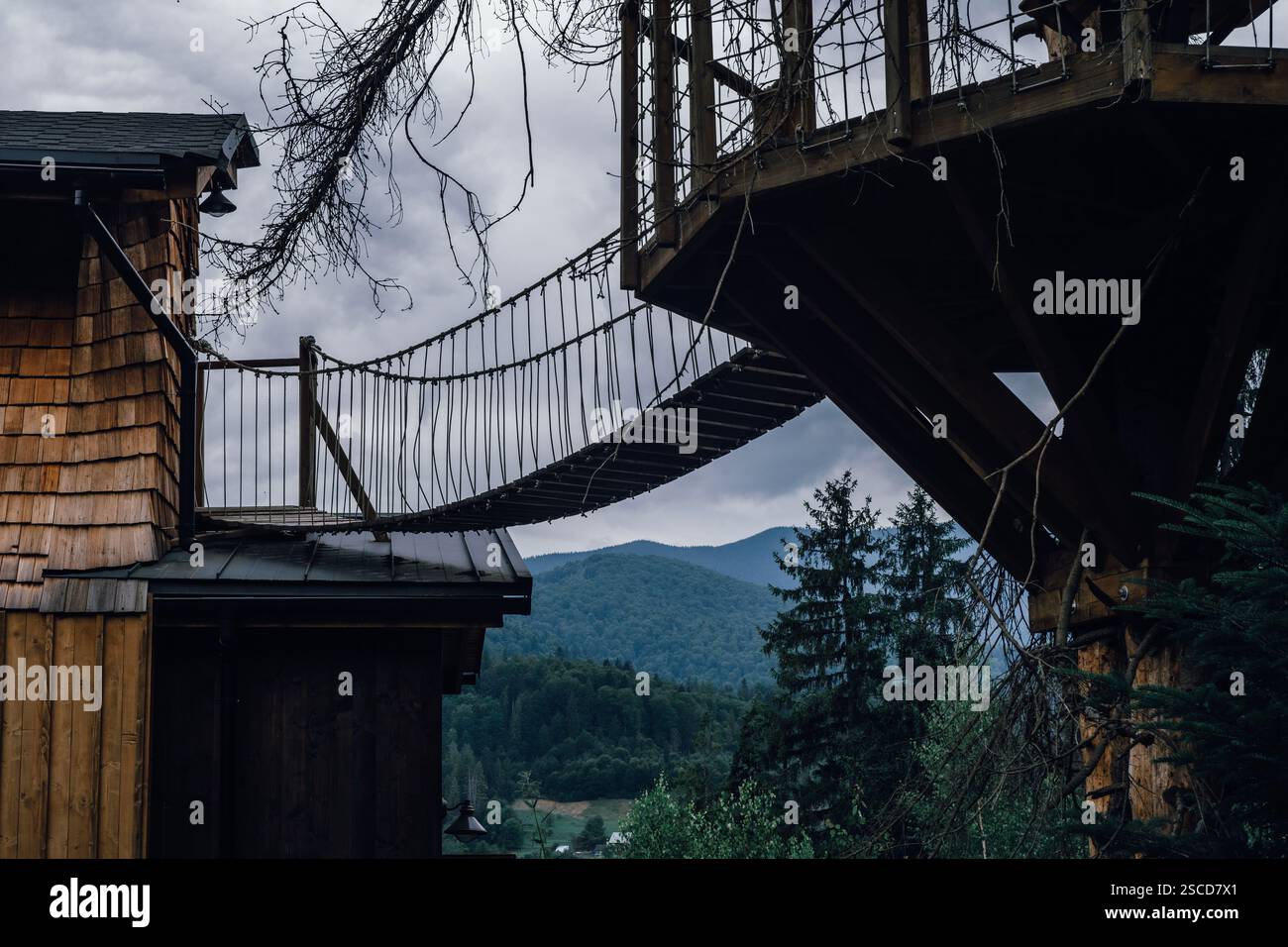 A cozy wooden treehouse, complete with a suspended bridge, blends into ...