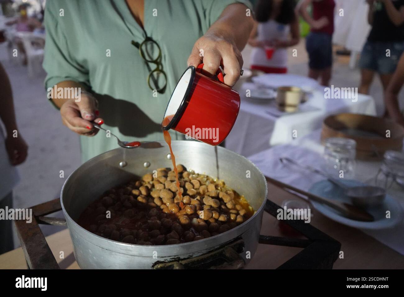 A woman pours tomato paste and juice into a pot with "topia", food that ...