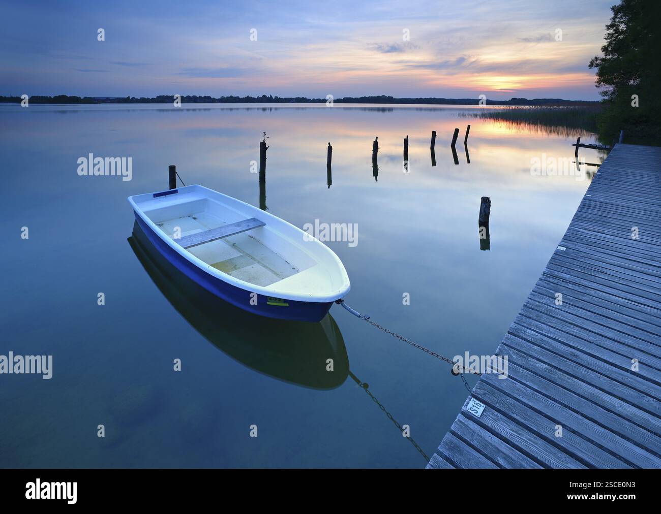 Sunset at Lake Schaalsee, jetty with rowing boat and wooden post in the ...