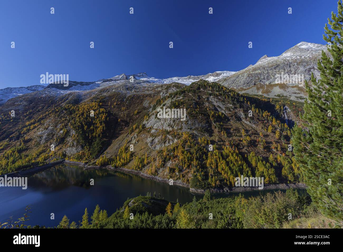 The Galgenbichl reservoir with a mountain forest in fall foliage on a ...