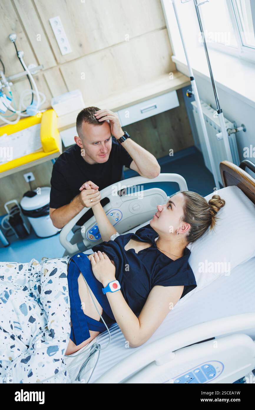 A man holds the hand of his wife who is giving birth to a child. The ...