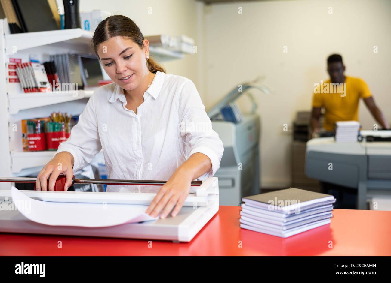 Portrait of happy young female typographer using paper cutter cutter ...