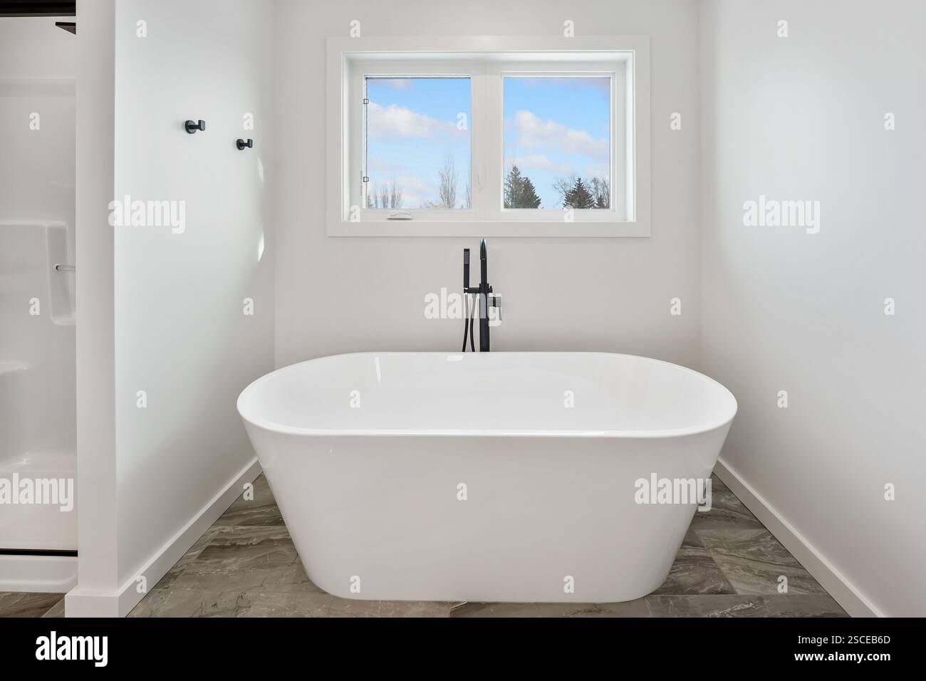A white bathtub with a black faucet sits in a bathroom with a window ...