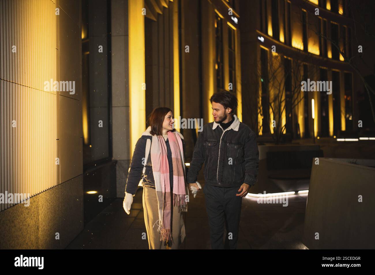 A couple walks and chats happily through a warmly lit city street at ...