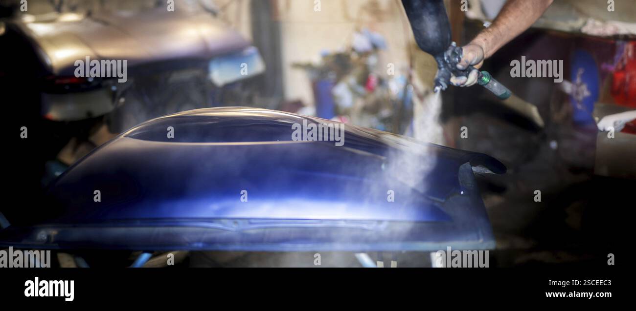A car part being painted with a spray gun in an automotive workshop ...