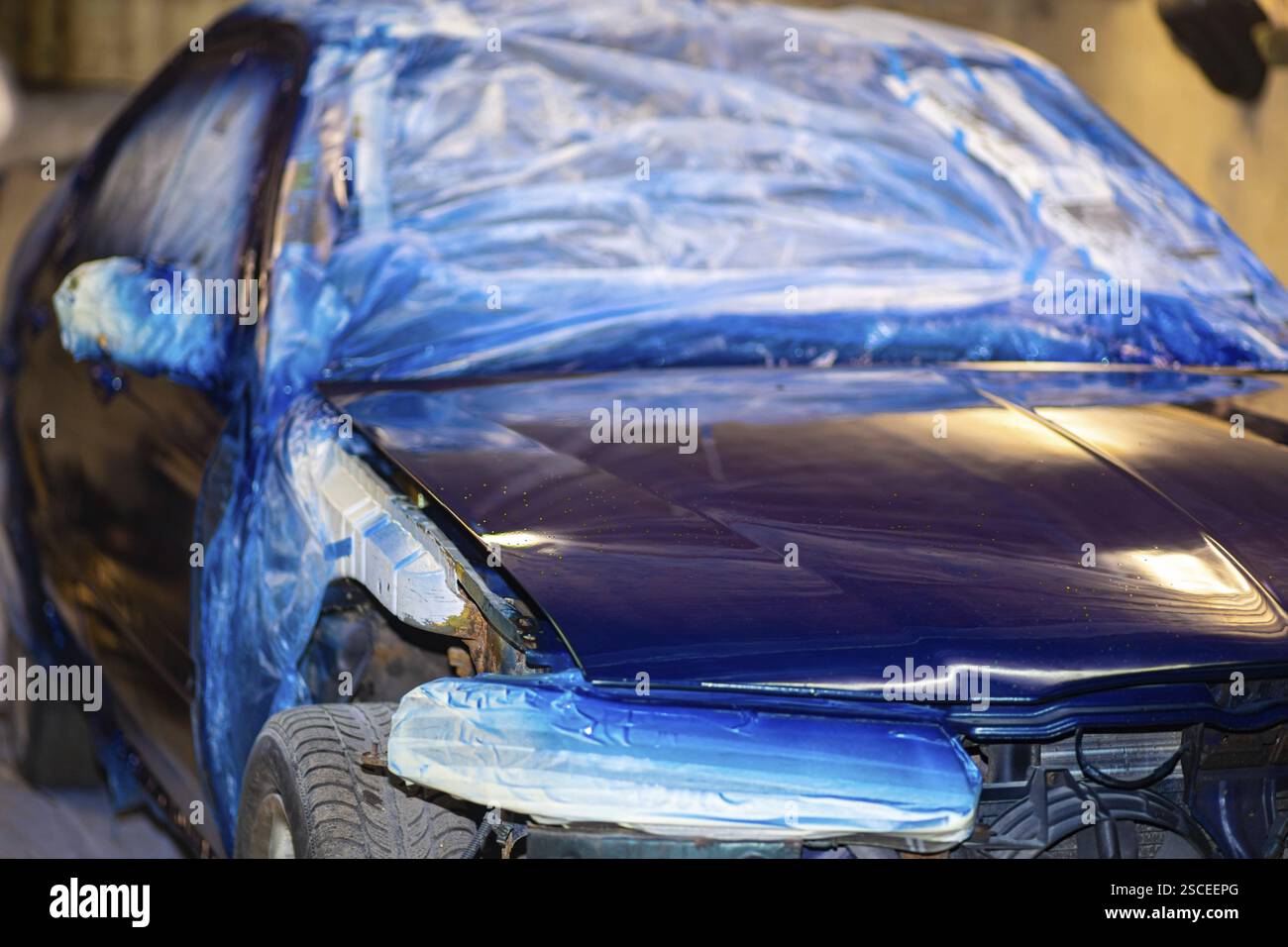 A blue car partially covered with plastic sheeting in a workshop ...