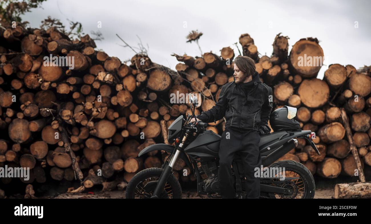 Individual on a motorcycle beside log piles in a natural, rugged ...