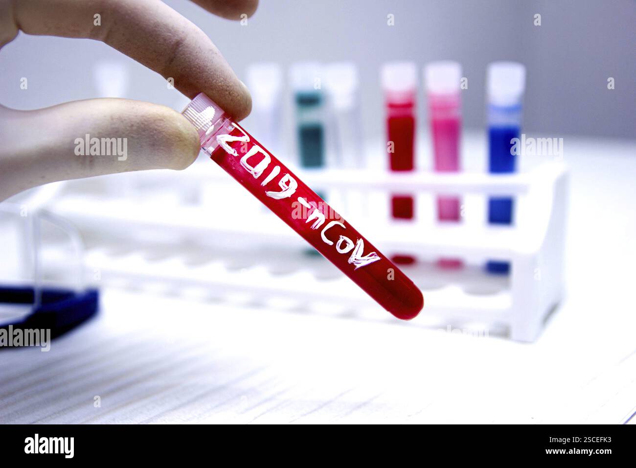 A hand raising a test tube labeled 2019-nCoV in front of colored test ...